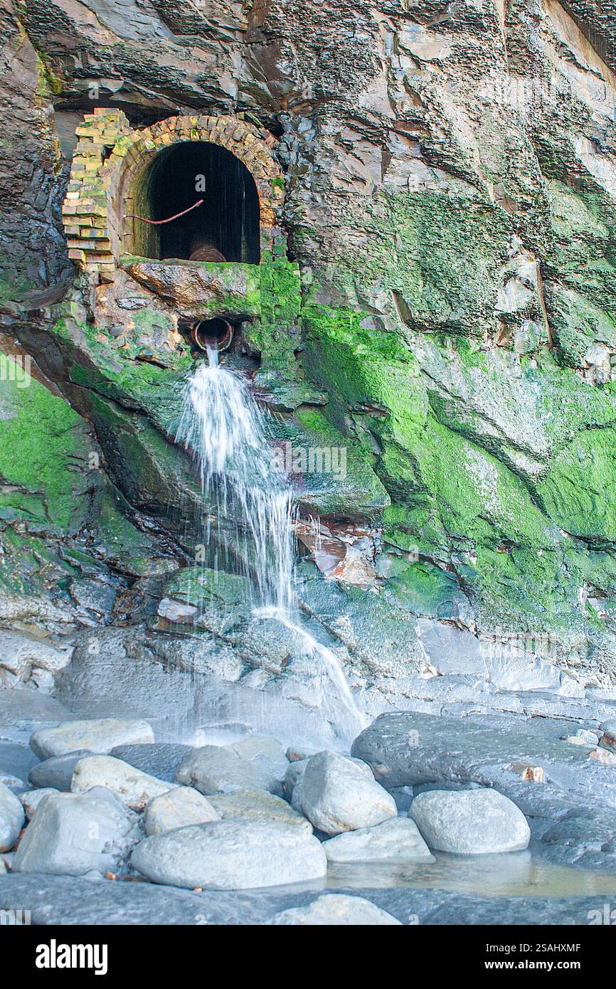 water flowing from a pipe & brick arch inside a cliff face Stock Photo ...