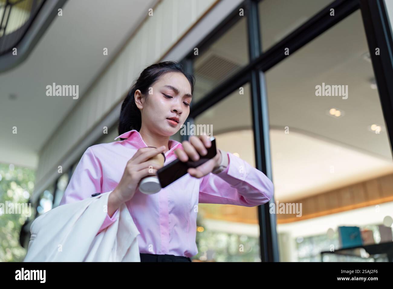 Focused Asian businesswoman checking her smartwatch while holding a ...