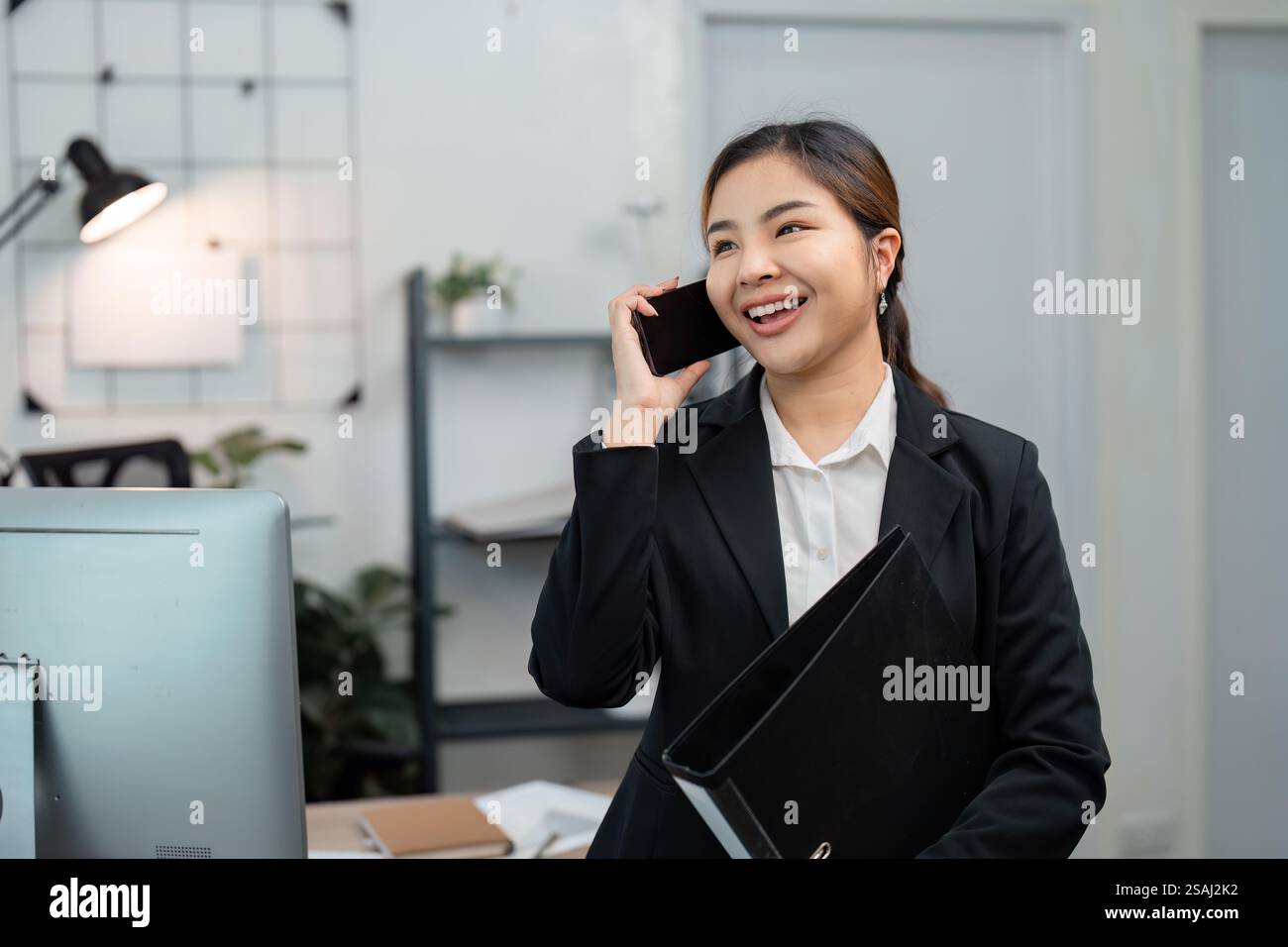 Enthusiastic Asian female call center agent talking on the phone while ...