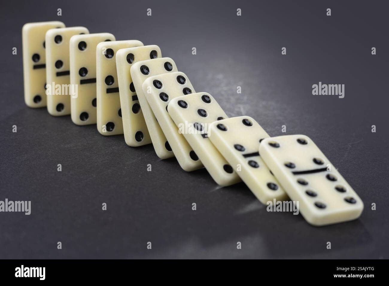 Domino effect concept with white dominoes pieces row falling on dark ...