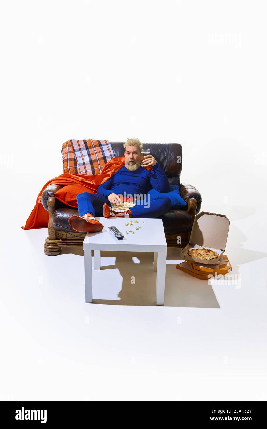 Man in superhero costume sitting on couch, watching TV, eating popcorn ...
