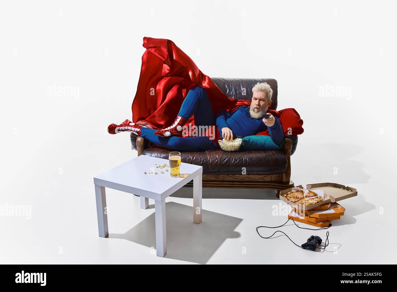 Man in superhero costume with red cape, lounging on couch with beer and ...