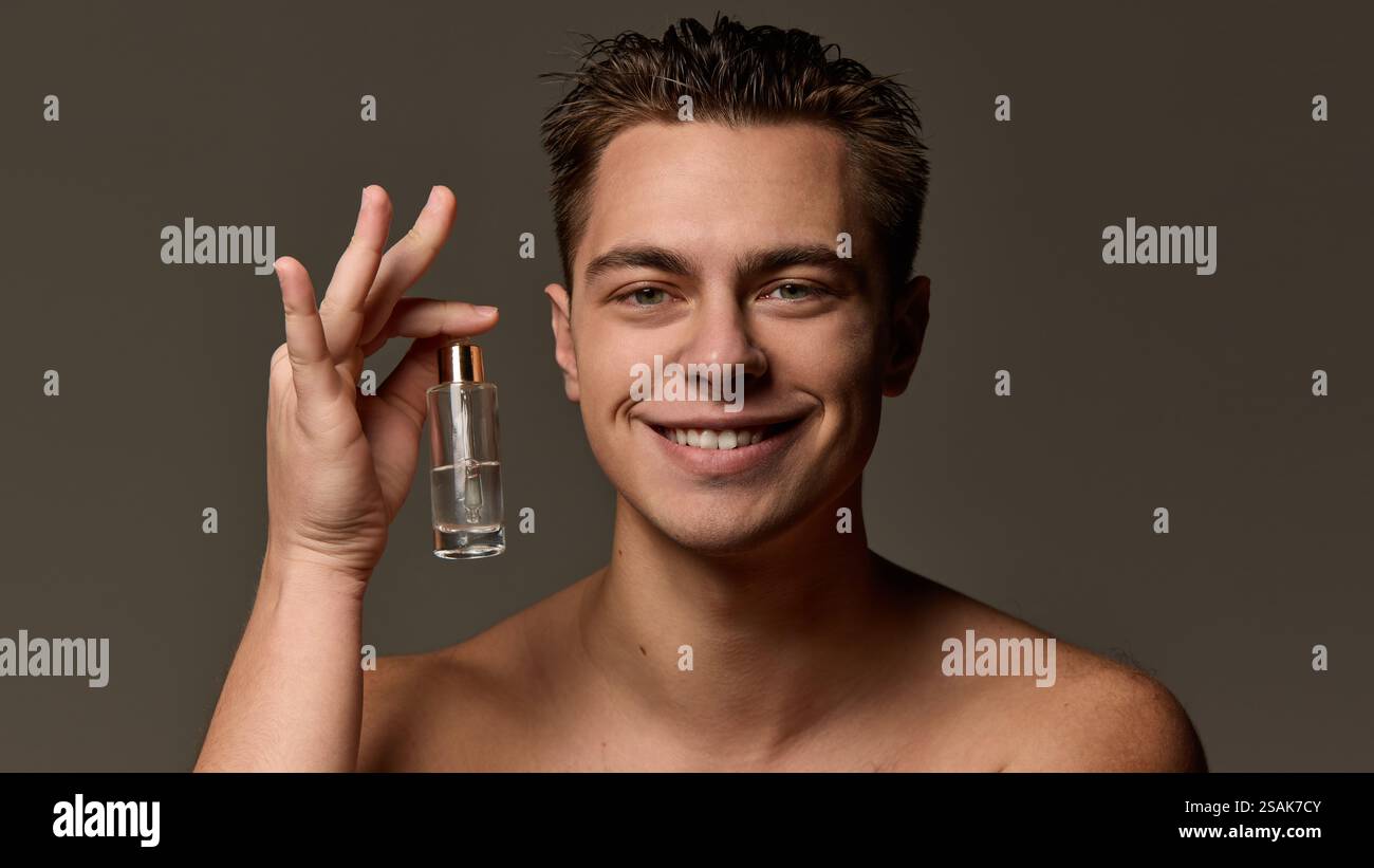 Man smiling while holding serum bottle between fingers, raising it ...