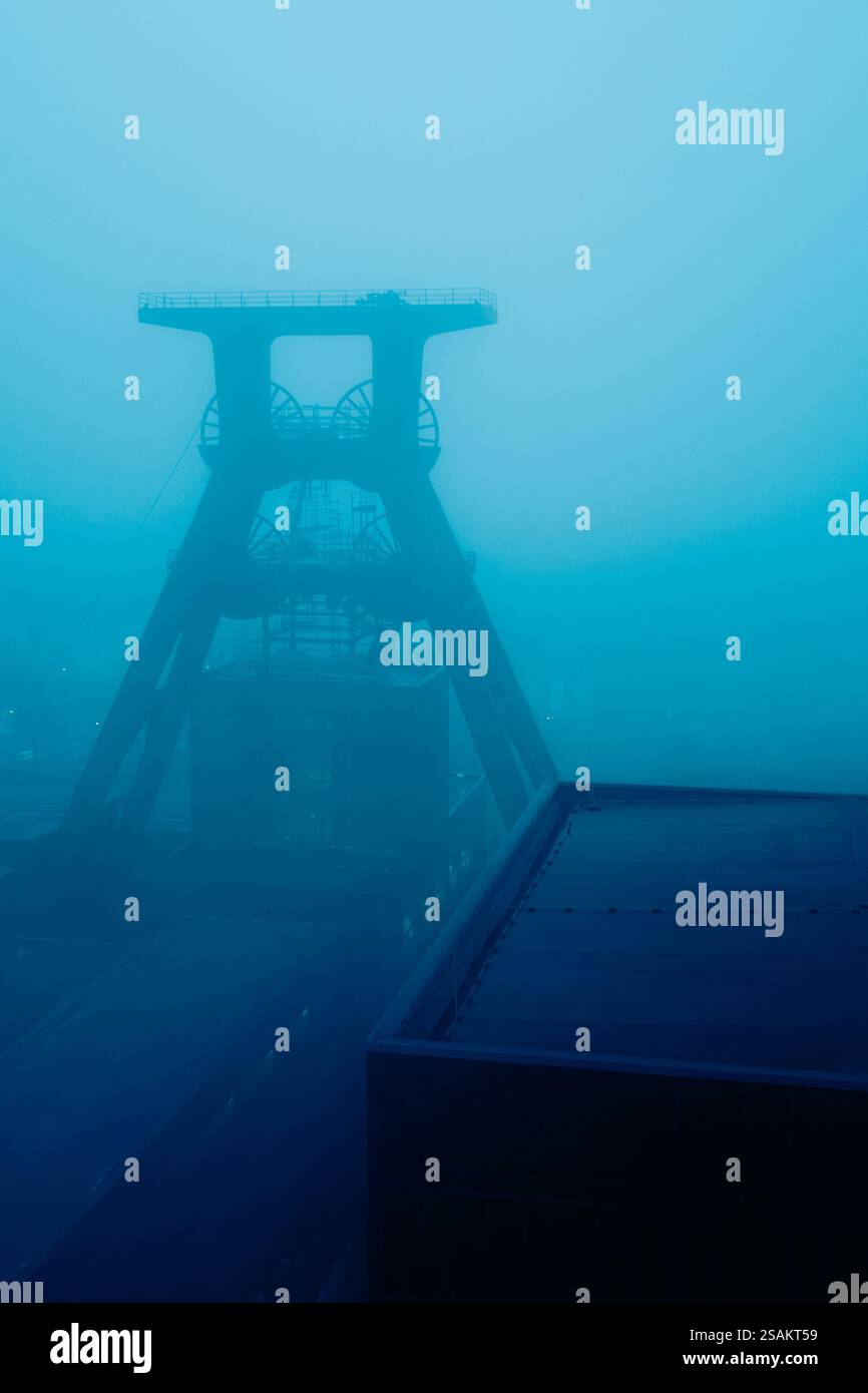 Industrial mining structure emerging through dense blue fog, creating a ...