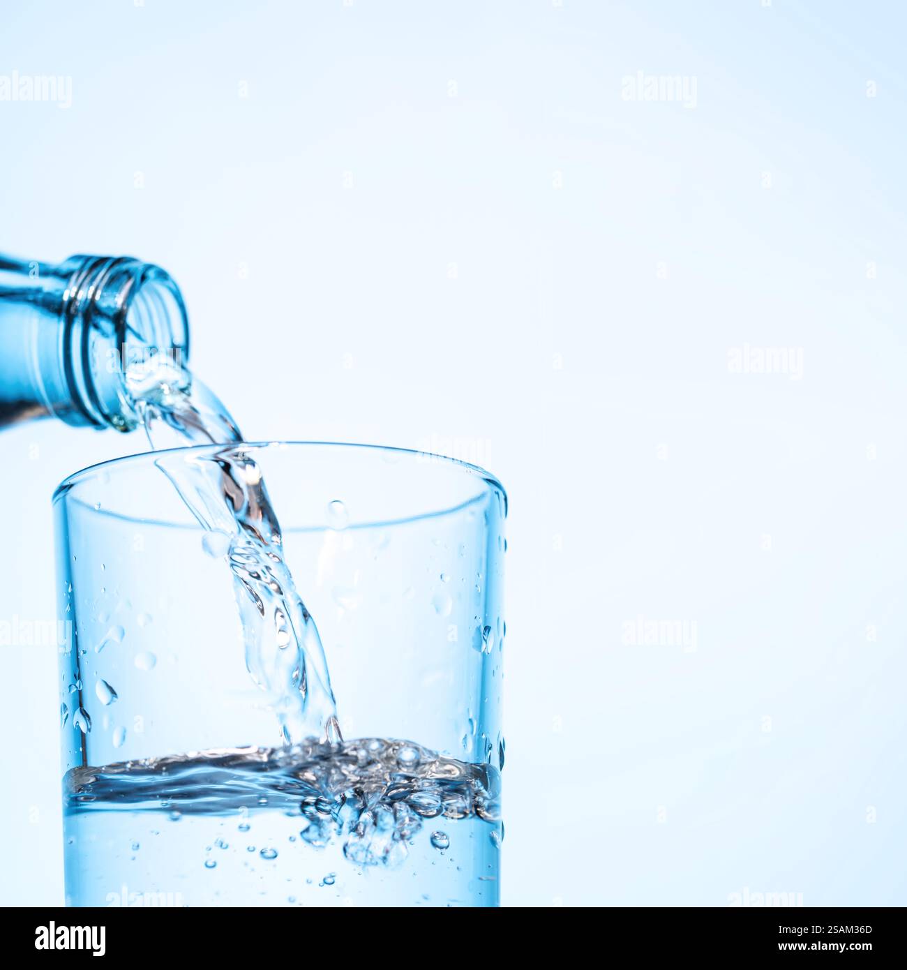 Crystal clear water being poured into a transparent glass with ice, creating refreshing ripples ...