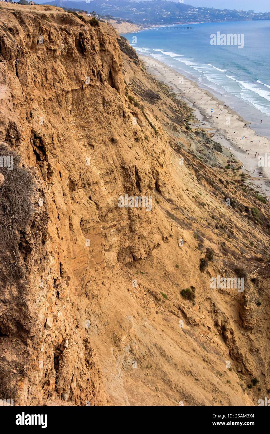 A rocky cliff overlooks a beach with people walking on the sand. The ...
