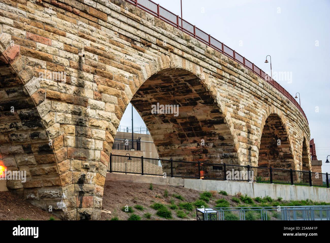 A stone arch bridge with a red railing. The bridge is old and has a ...