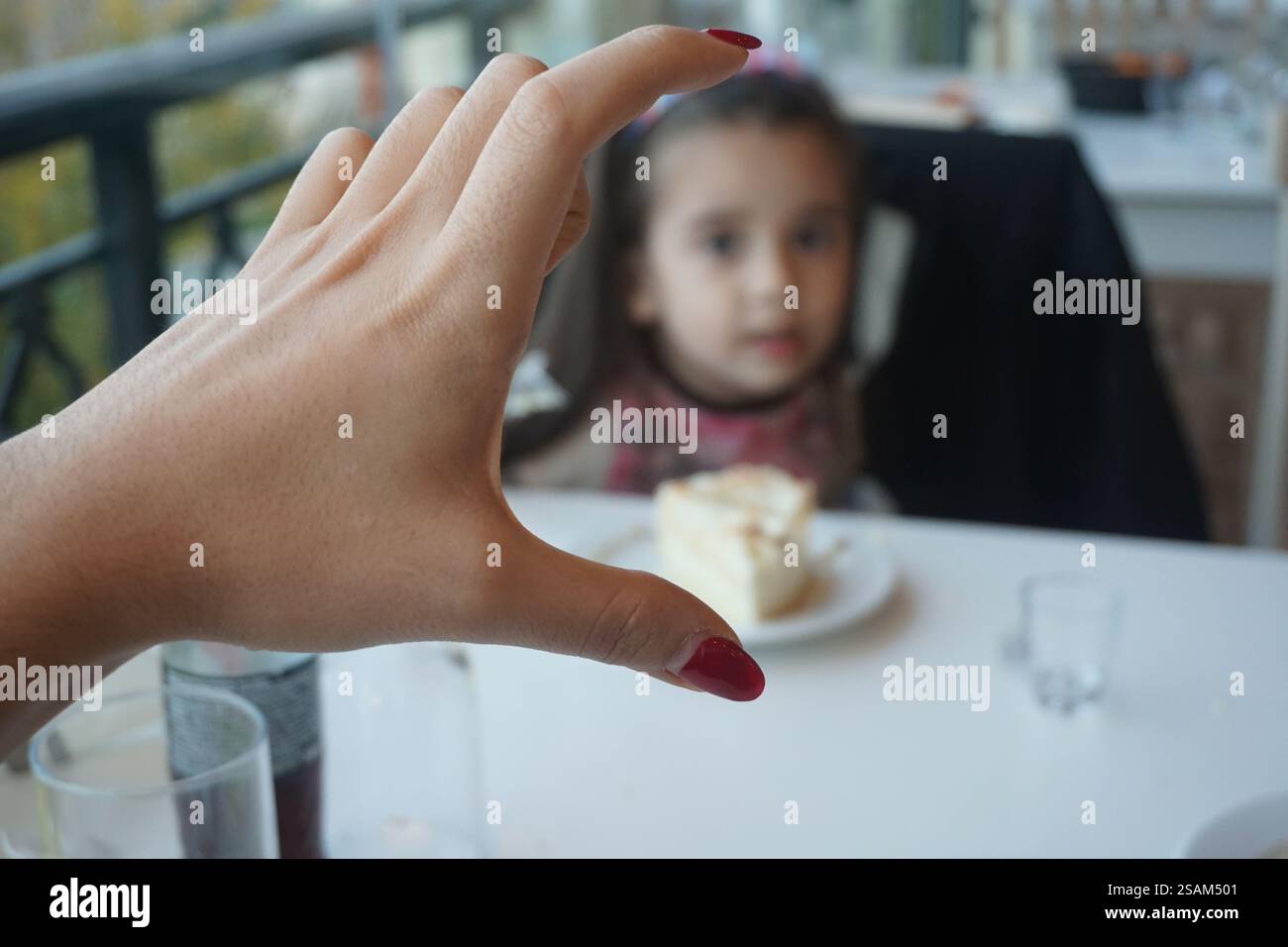 A young woman forms a heart with her hand to enclose a two-year-old ...