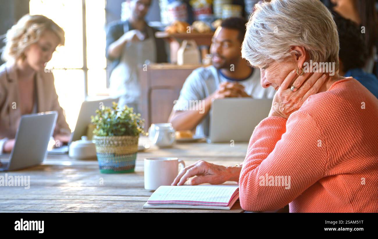 Senior Female Customer In Coffee Shop Sitting At Table With Drink ...