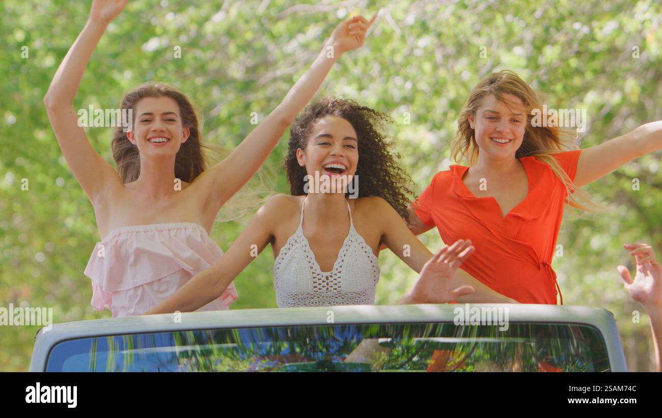 Group Of Young Friends On Road Trip Driving In Convertible Car With ...