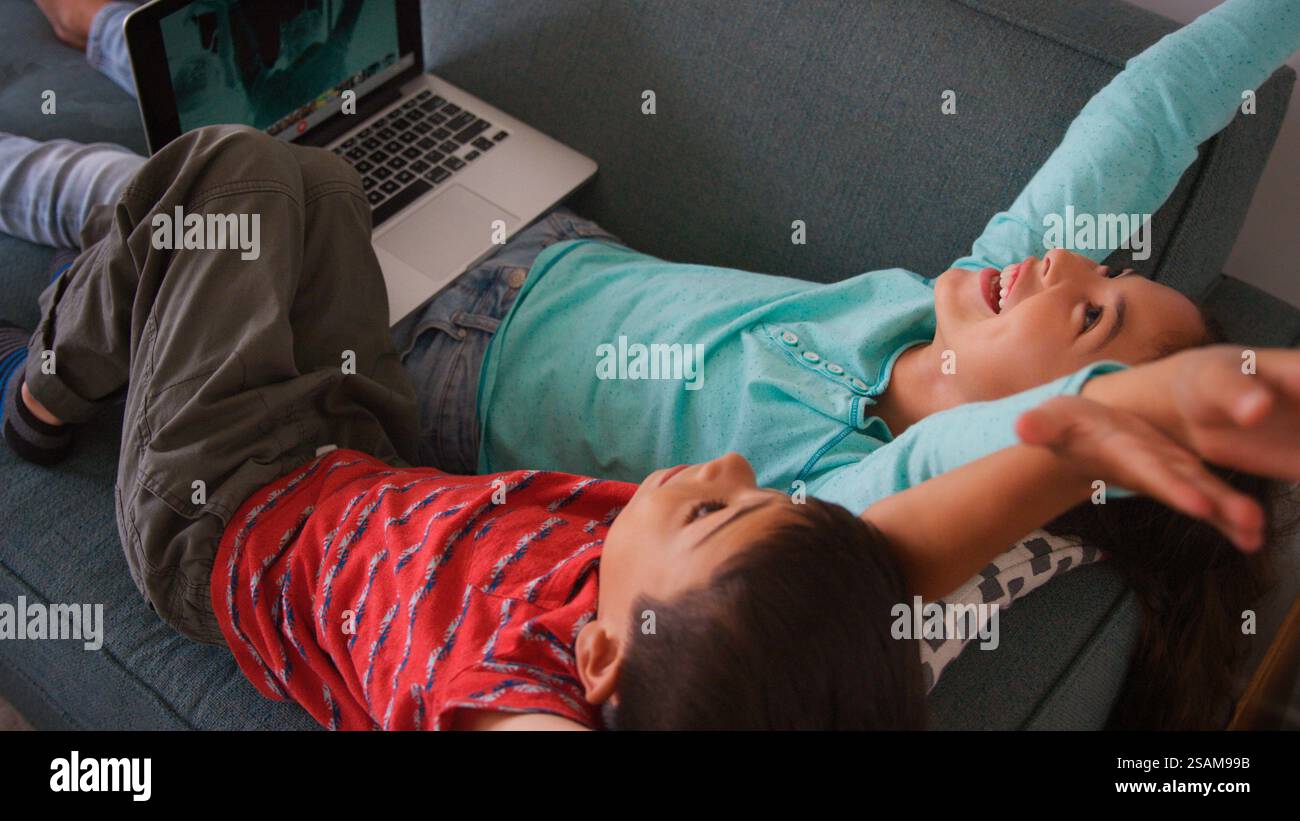 Over The Shoulder Shot Brother And Sister Sitting On Sofa At Home Using ...