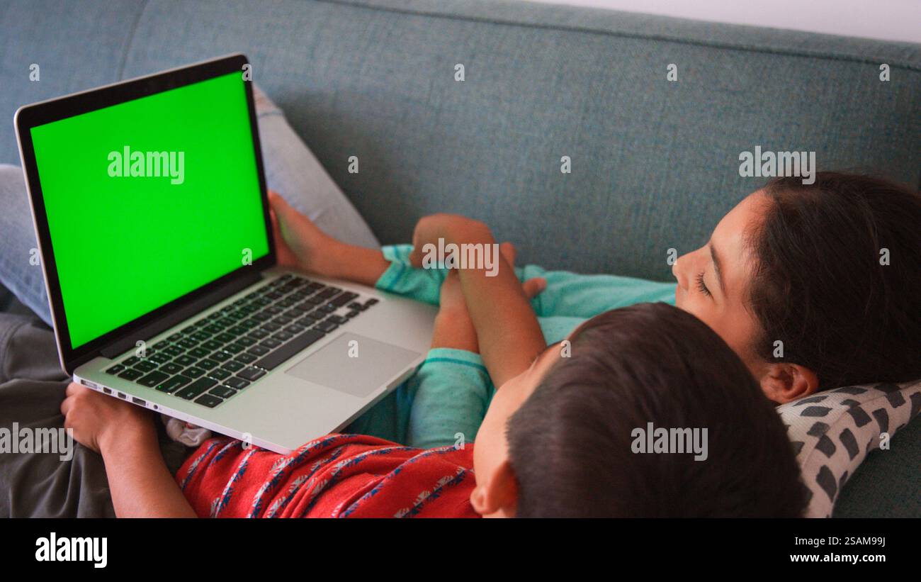 Rear View Shot Of Two Children Sitting On Sofa At Home Using Green ...