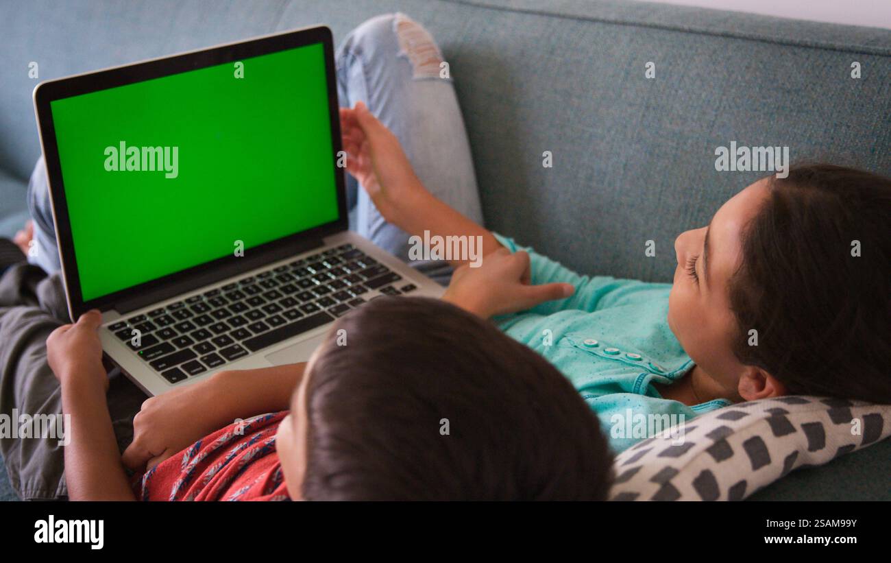 Rear View Shot Of Two Children Sitting On Sofa At Home Using Green ...