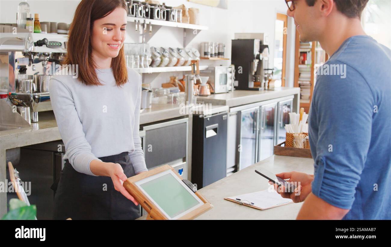 Female Worker Behind Counter Taking Contactless Payment From Male ...