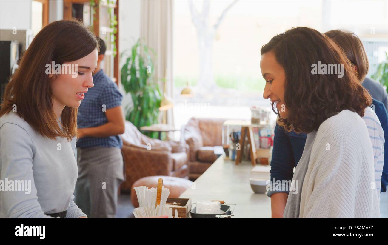 Female Worker Behind Counter Serving Female Customer In Busy Coffee ...