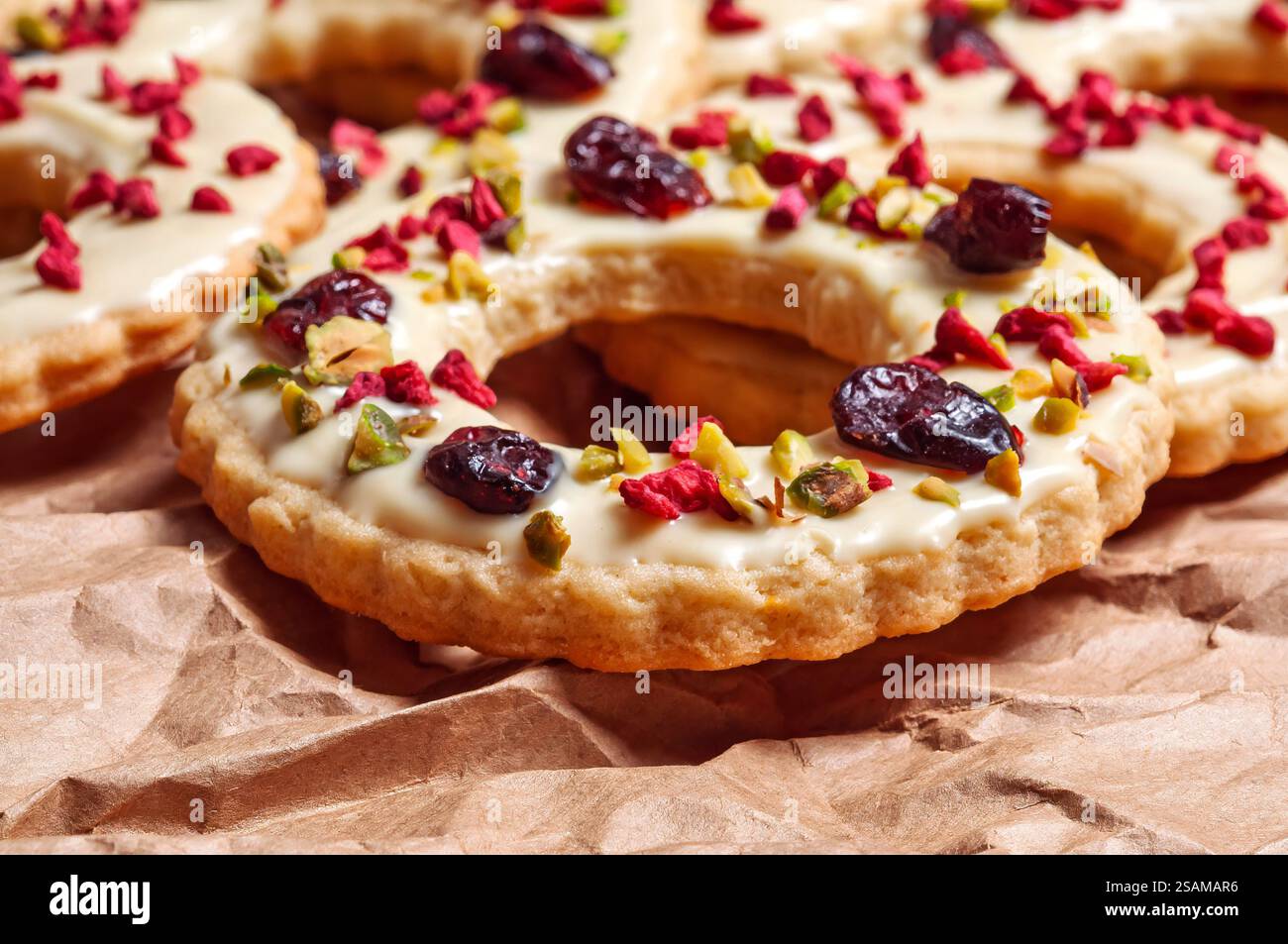 Festive cookies topped with dried fruits, nuts, and icing on a textured ...