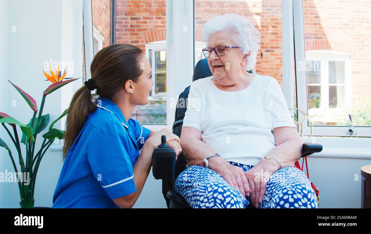 Senior Woman Sitting In Chair In Residents Lounge And Talking With ...