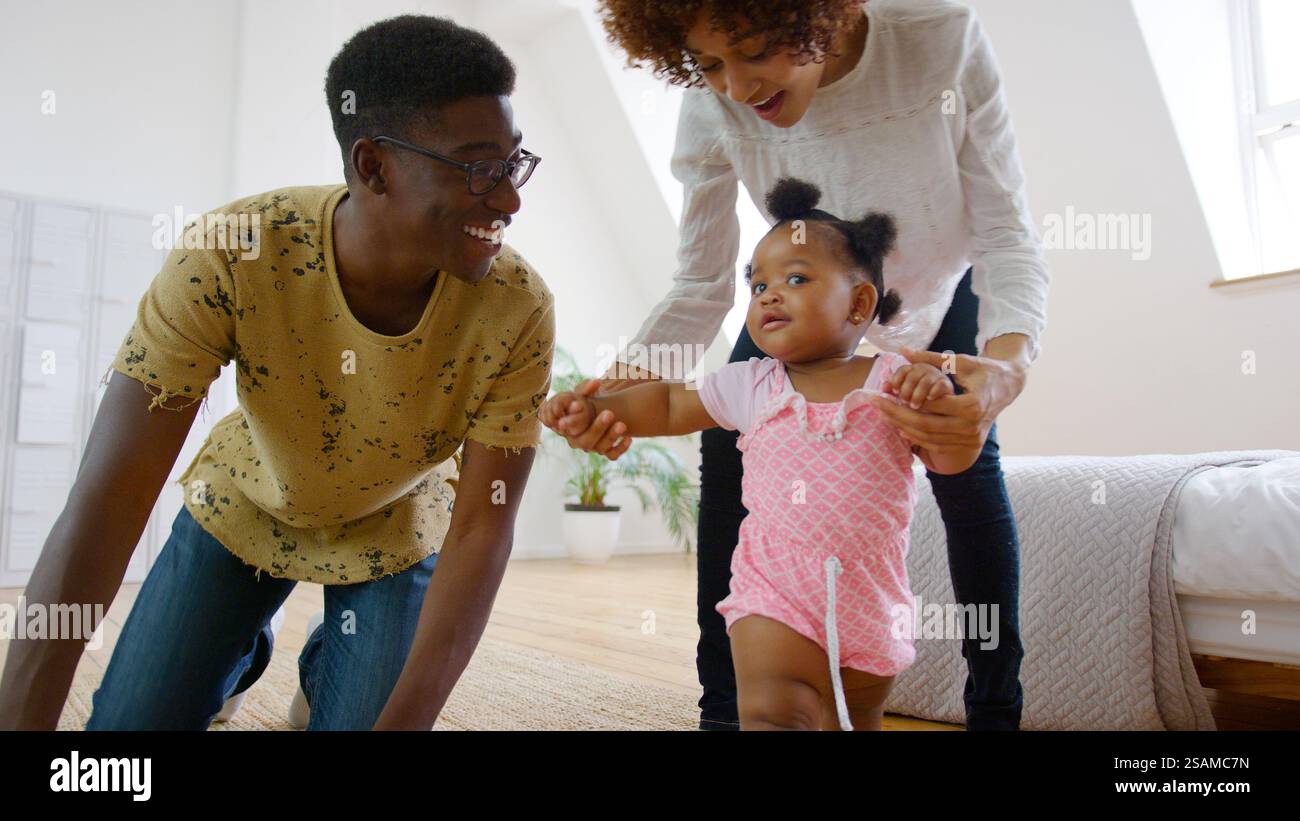 Baby Girl Learning To Walk At Home As Parents Help And Give ...