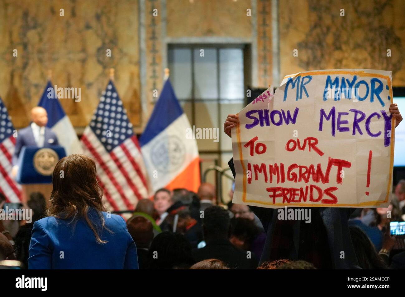 People hold up a sign as New York City mayor Eric Adams starts to speak ...
