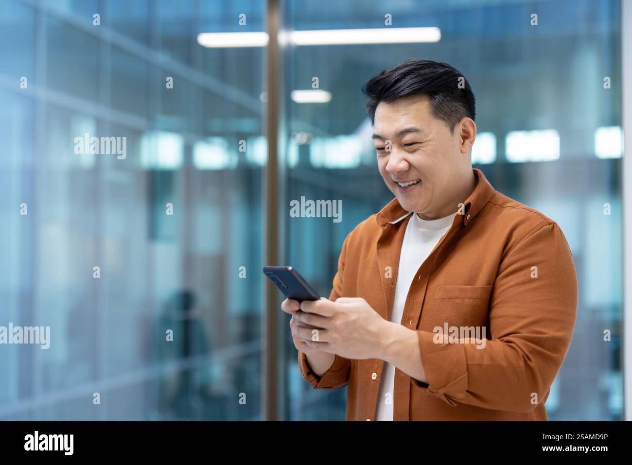 Successful Asian businessman standing near the window with phone in ...