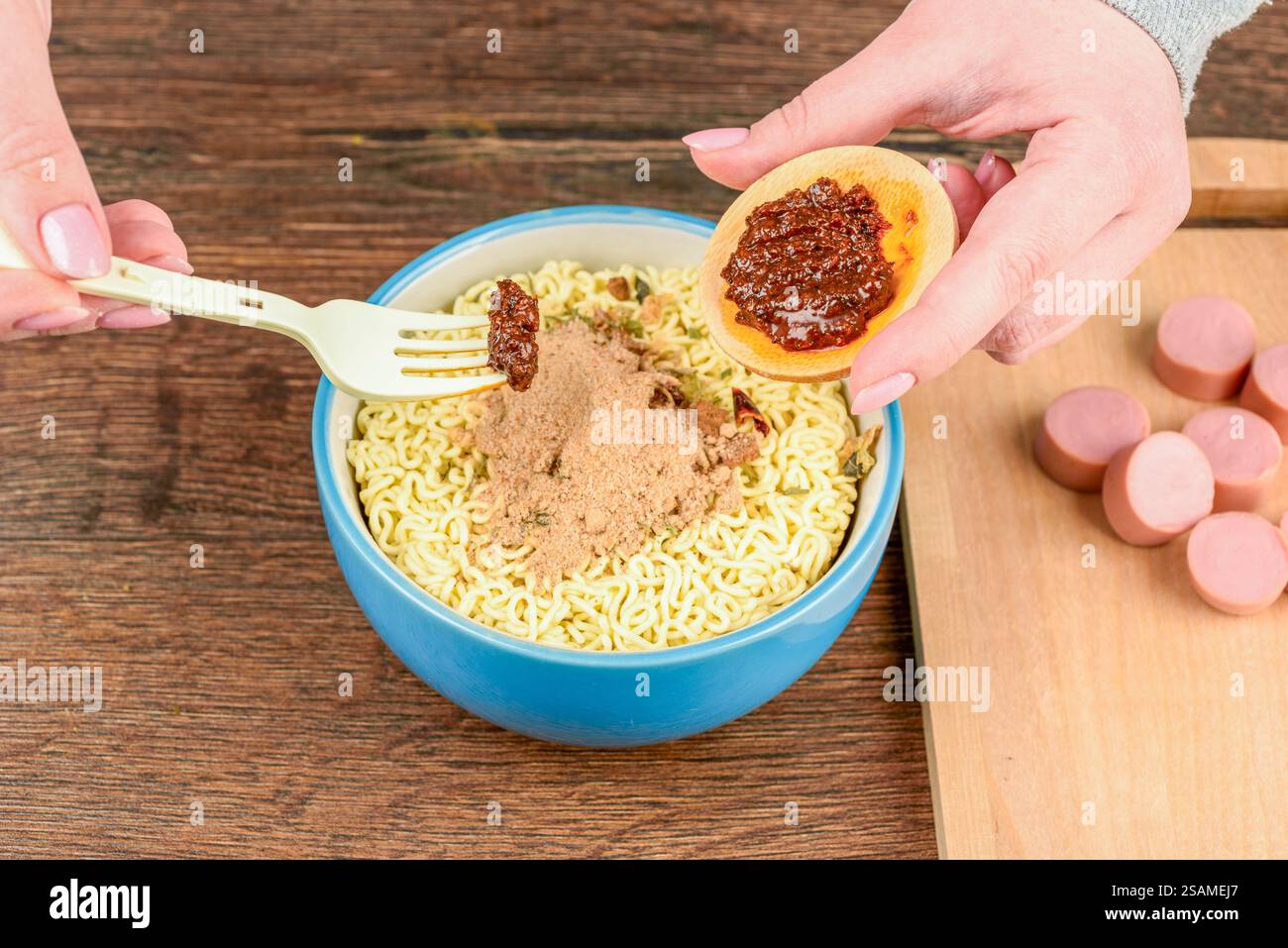 A woman spoons sauce from a saucer on instant noodles using a fork ...