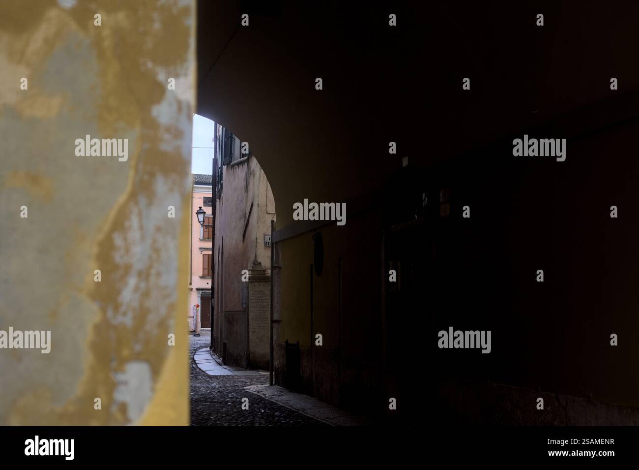 Narrow alley in the shade under an arch framed by a wall in an italian ...