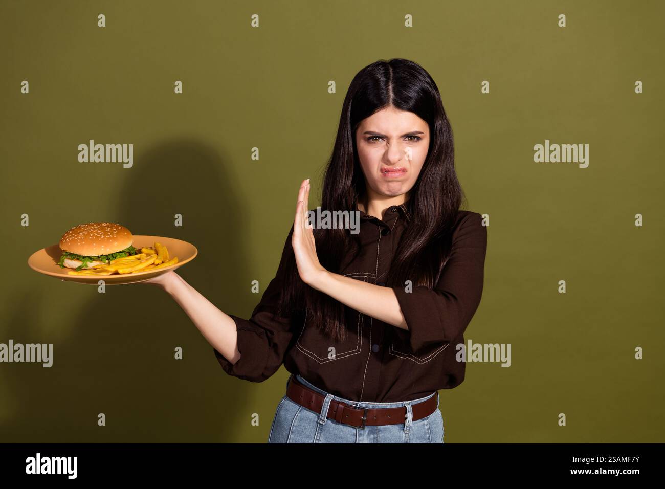 Young woman showing disgust at a plate of food with a green background ...