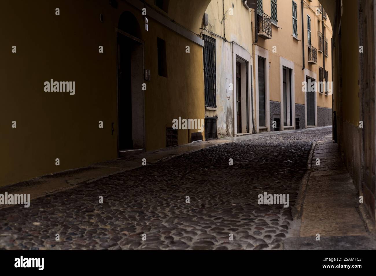 Narrow alley in the shade under an arch framed by a wall in an italian ...