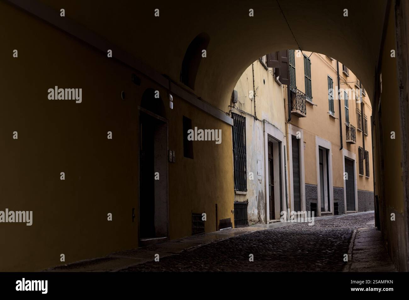 Narrow alley in the shade under an arch framed by a wall in an italian ...