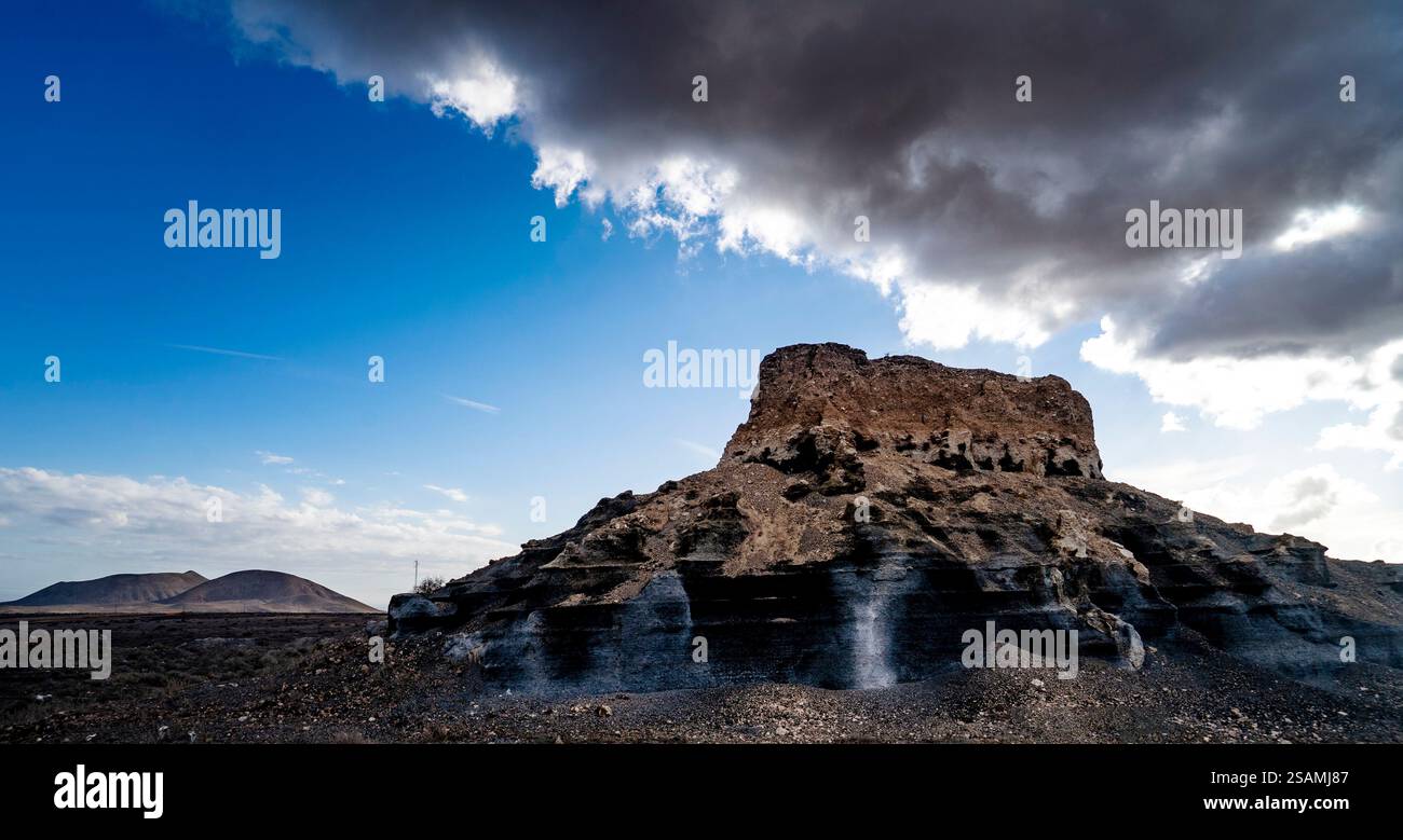 A rugged rock formation rises against a dramatic sky with scattered ...