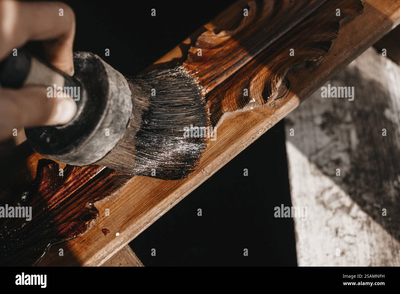 A brush applying varnish to a carved wood surface with a dark shadow ...