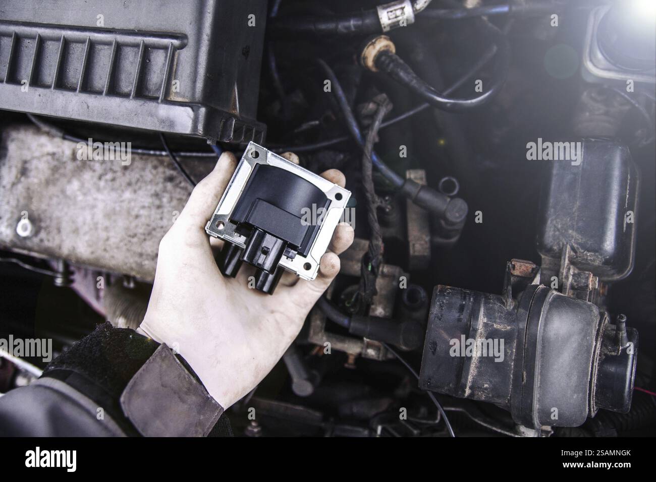 Hand holding a car part amidst various engine components and wiring ...