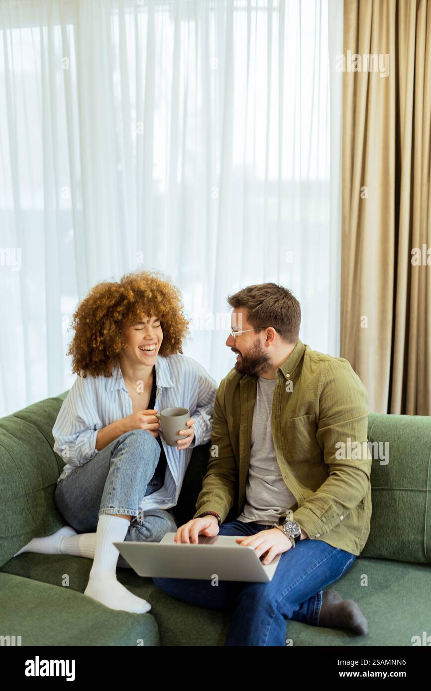 A cheerful couple sits side by side on a plush green couch, engaged in ...
