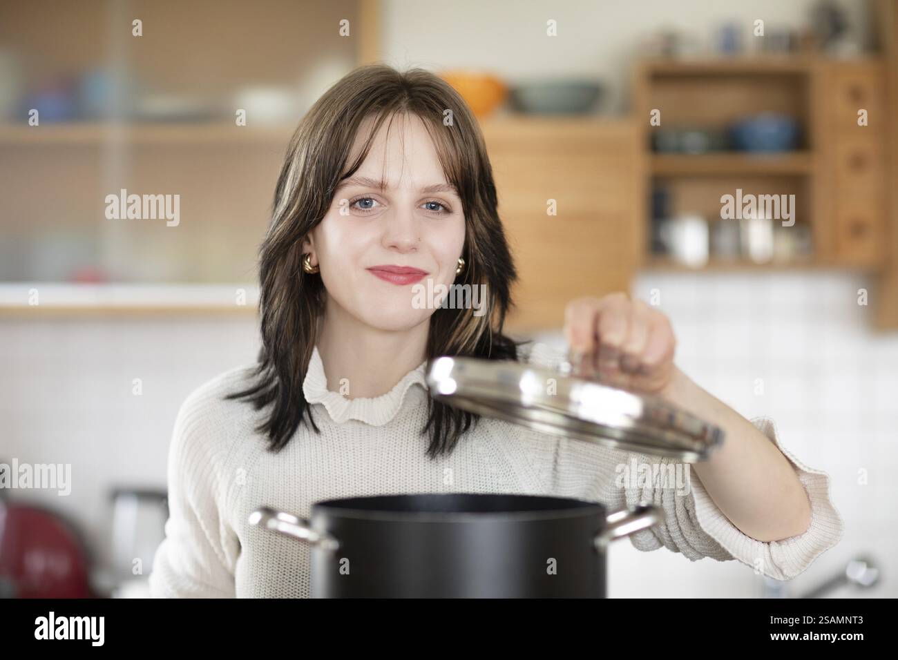Woman in the kitchen lifts the lid off a pot with a lid, energy saving ...