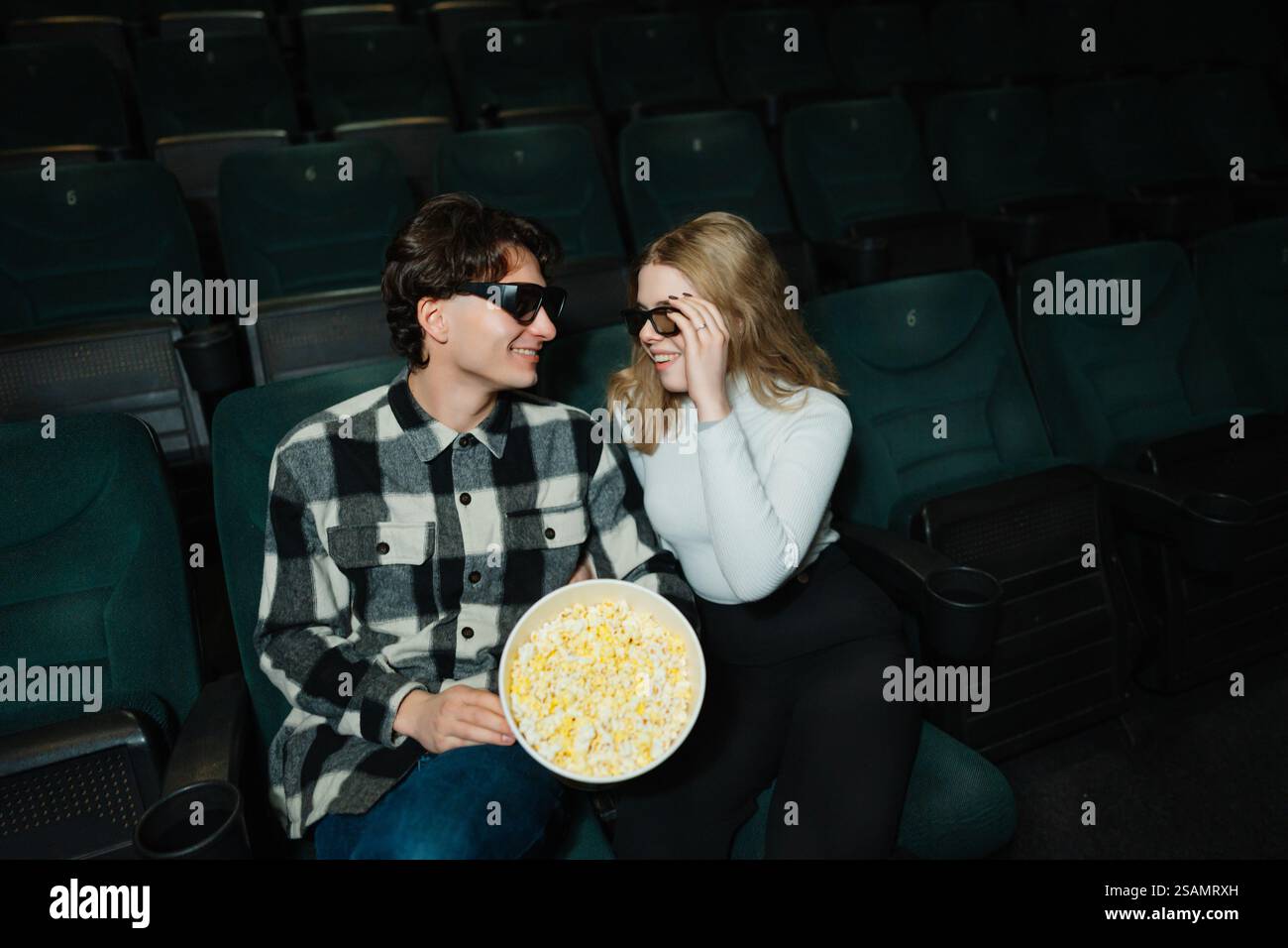 Couple enjoys popcorn together in a movie theater on a casual date ...