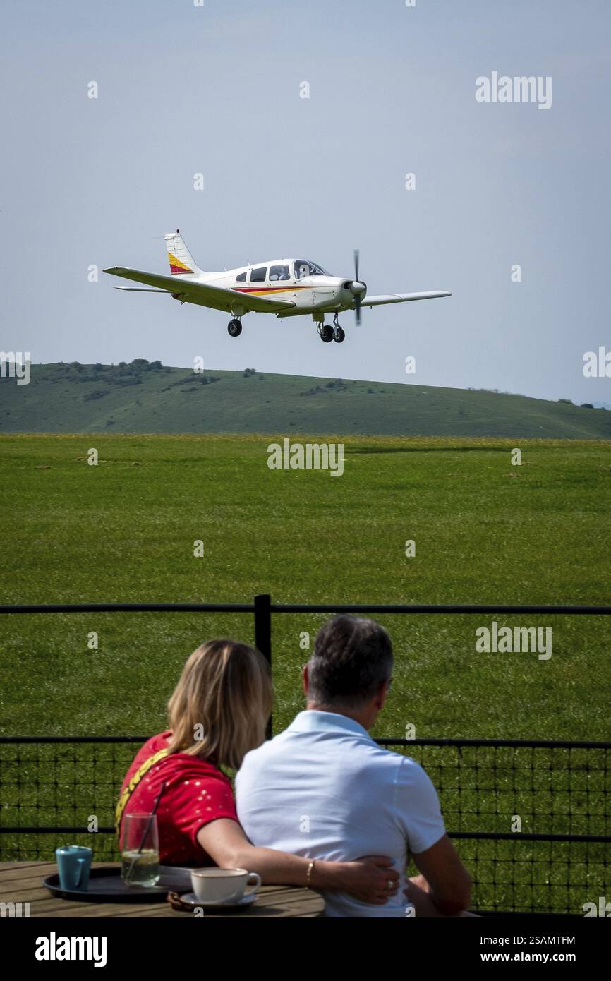A man and woman watch a Piper Warrior light aircraft landing at Compton ...