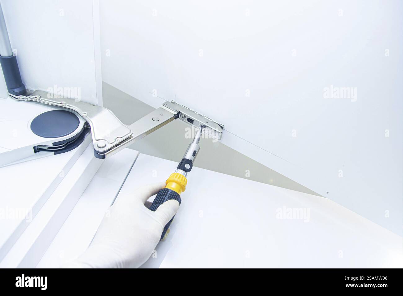Close-up of a gloved hand fixing a cabinet hinge with a screwdriver ...