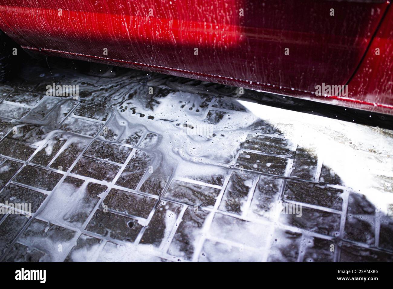Foamy soap water on pavement beneath a red car Stock Photo - Alamy