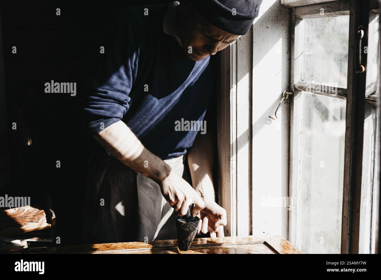 Person working on wood near a window with sunlight streaming in Stock ...