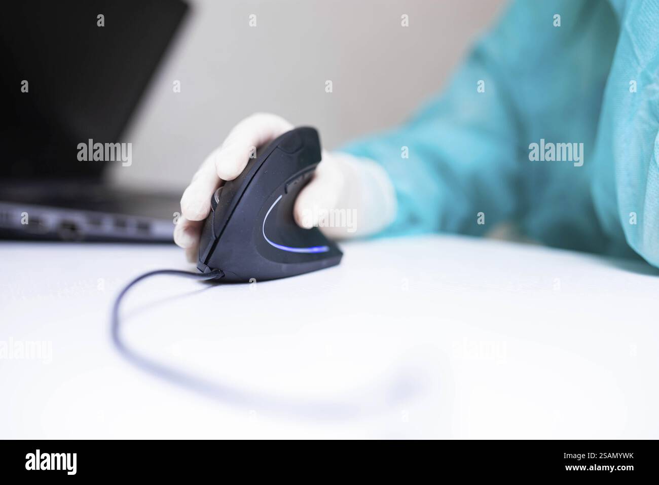 Gloved hand operating a computer mouse, with a laptop in the background ...