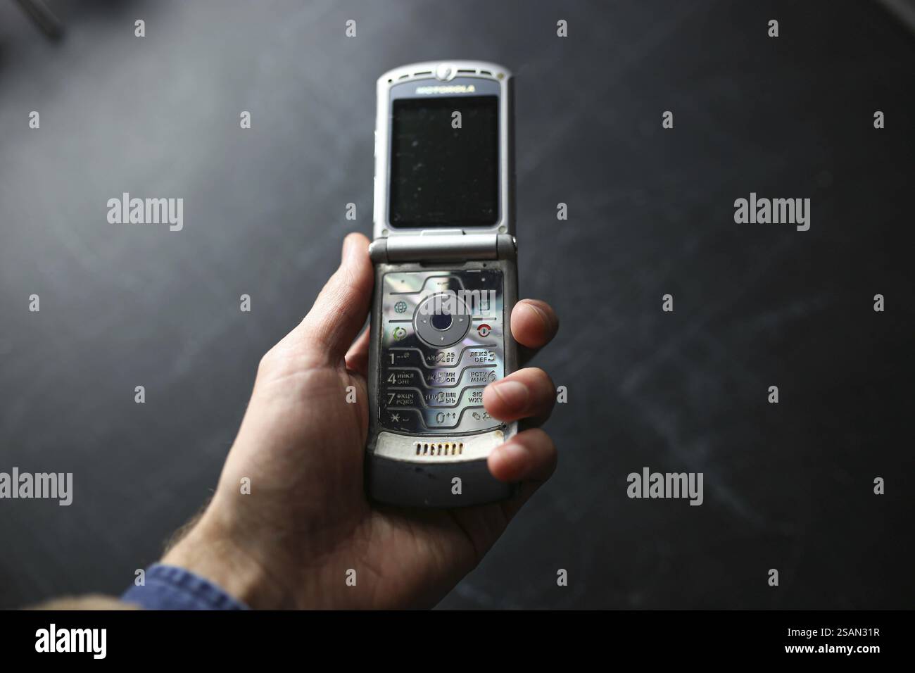 A classic flip phone opened in a hand with a dark backdrop Stock Photo ...