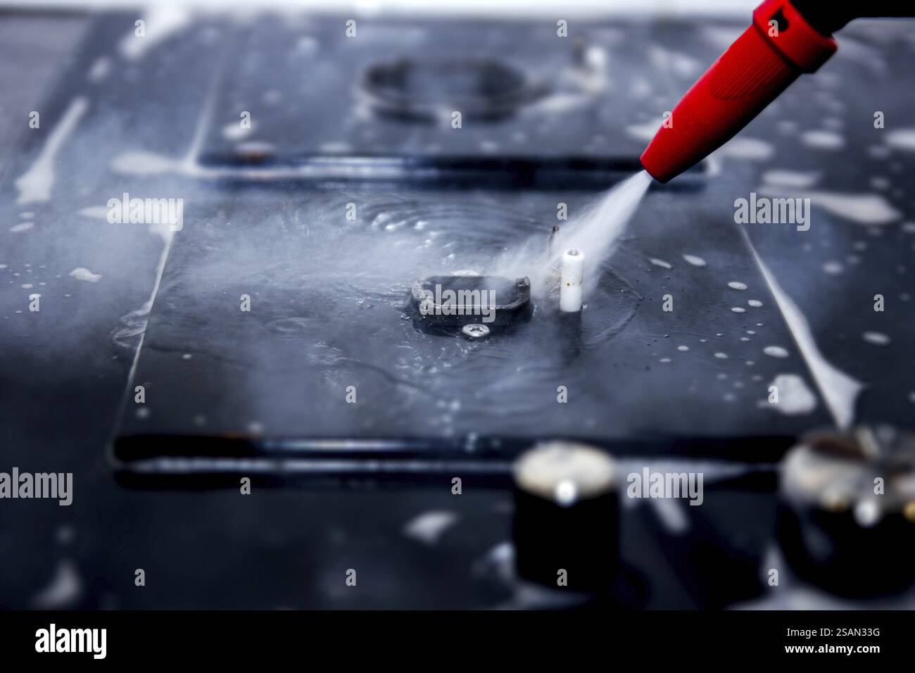 Water being sprayed onto a soapy stove surface from a red nozzle Stock ...