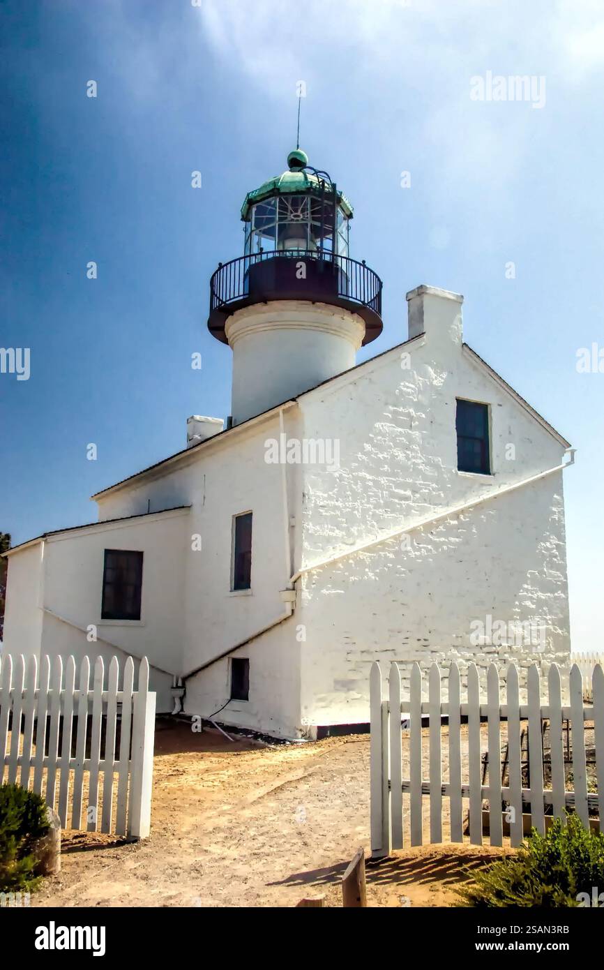 A white lighthouse with a green roof. The lighthouse is surrounded by a ...