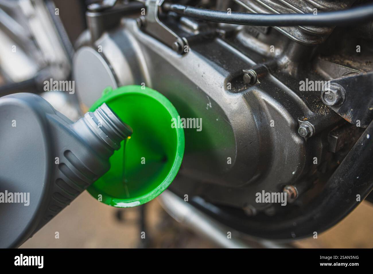 A close-up of a motorcycle engine with oil being poured through a green ...