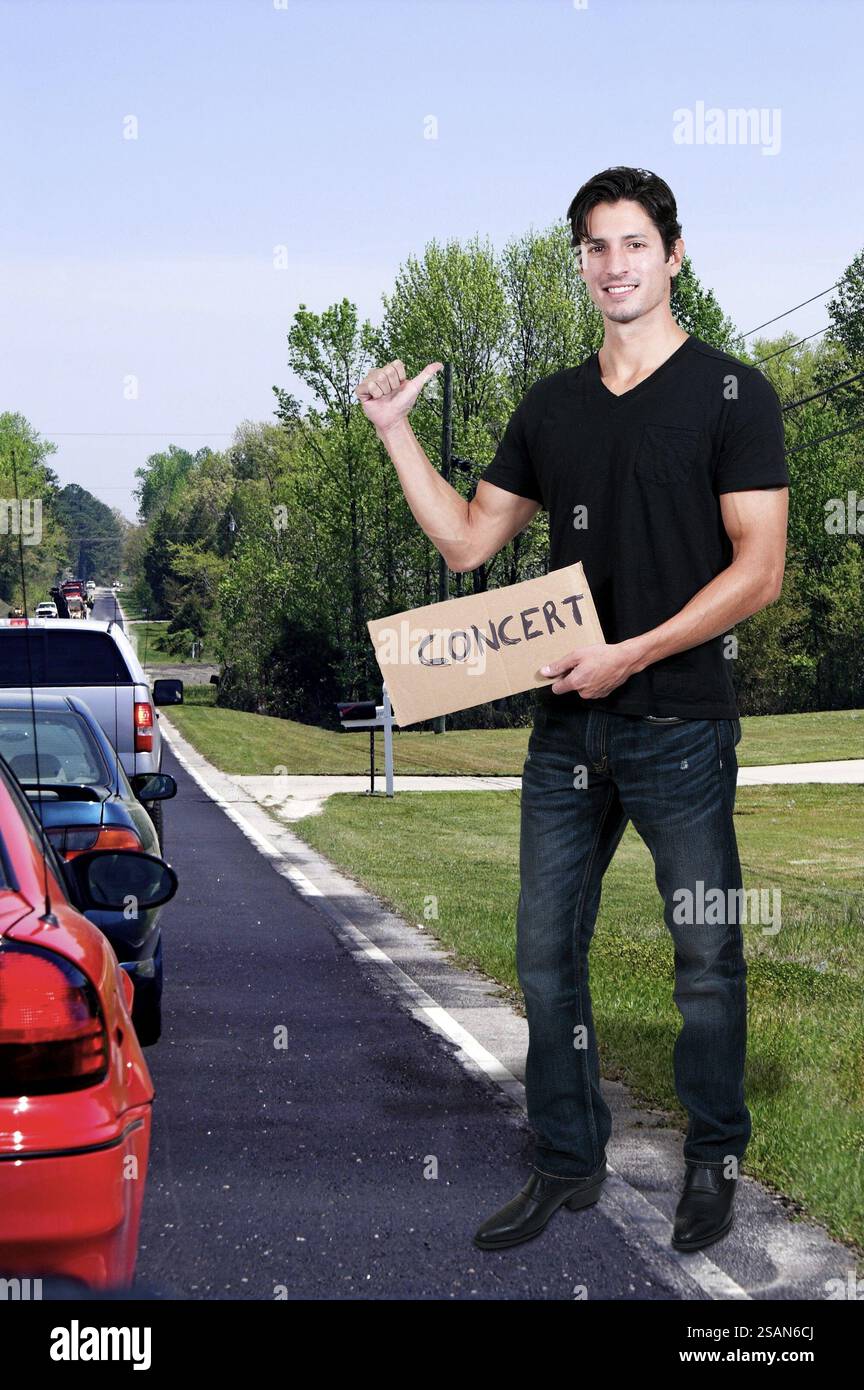 Handsome man with a sign hitch hiking to a concert Stock Photo - Alamy