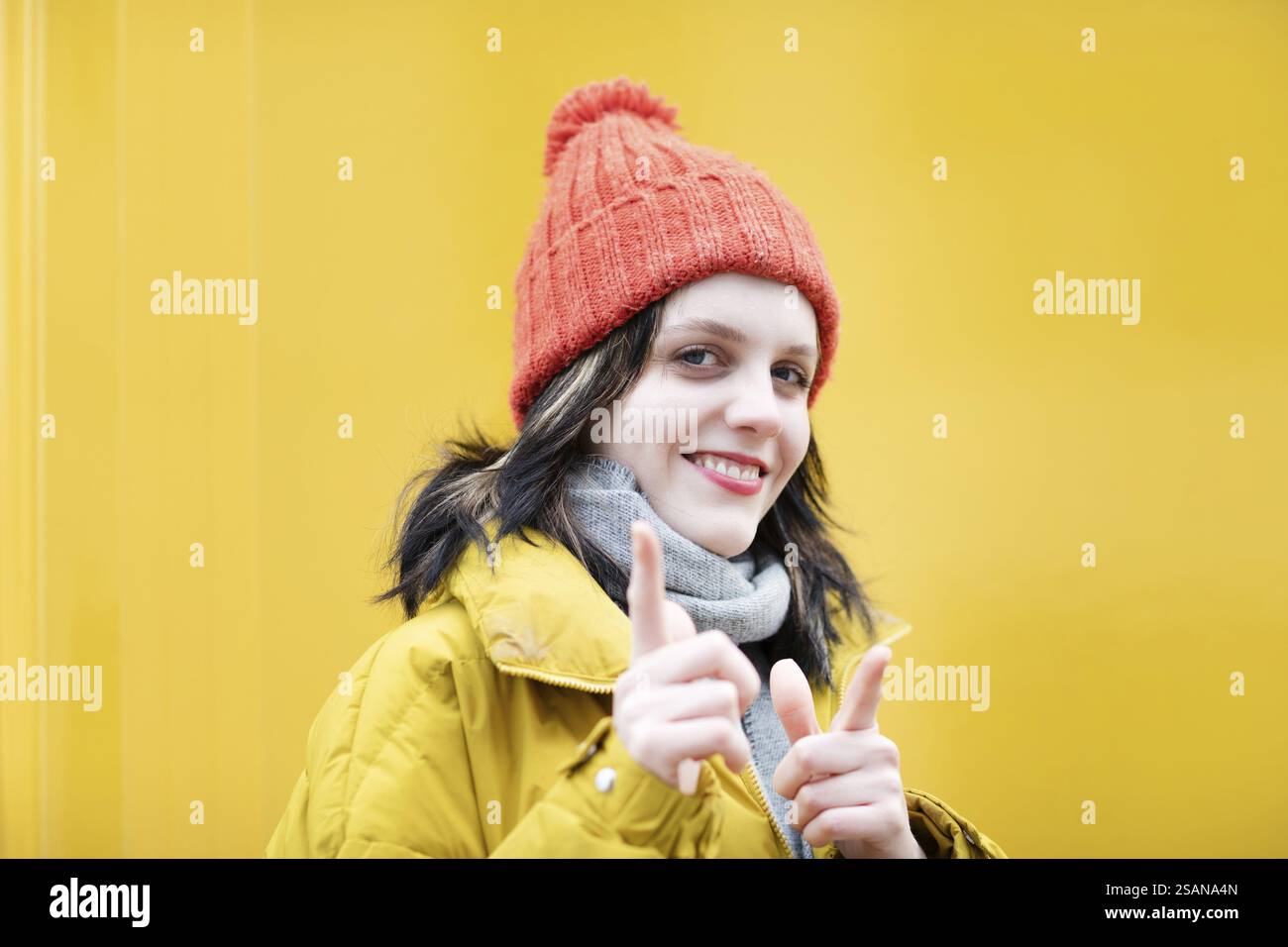 Smiling woman with finger pointing in front of yellow background ...