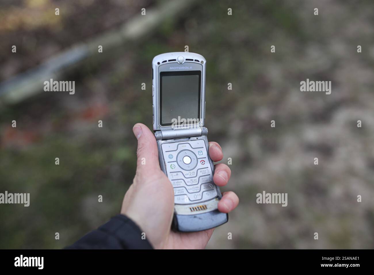 Open gray flip phone held in hand outdoors with slightly blurred ...