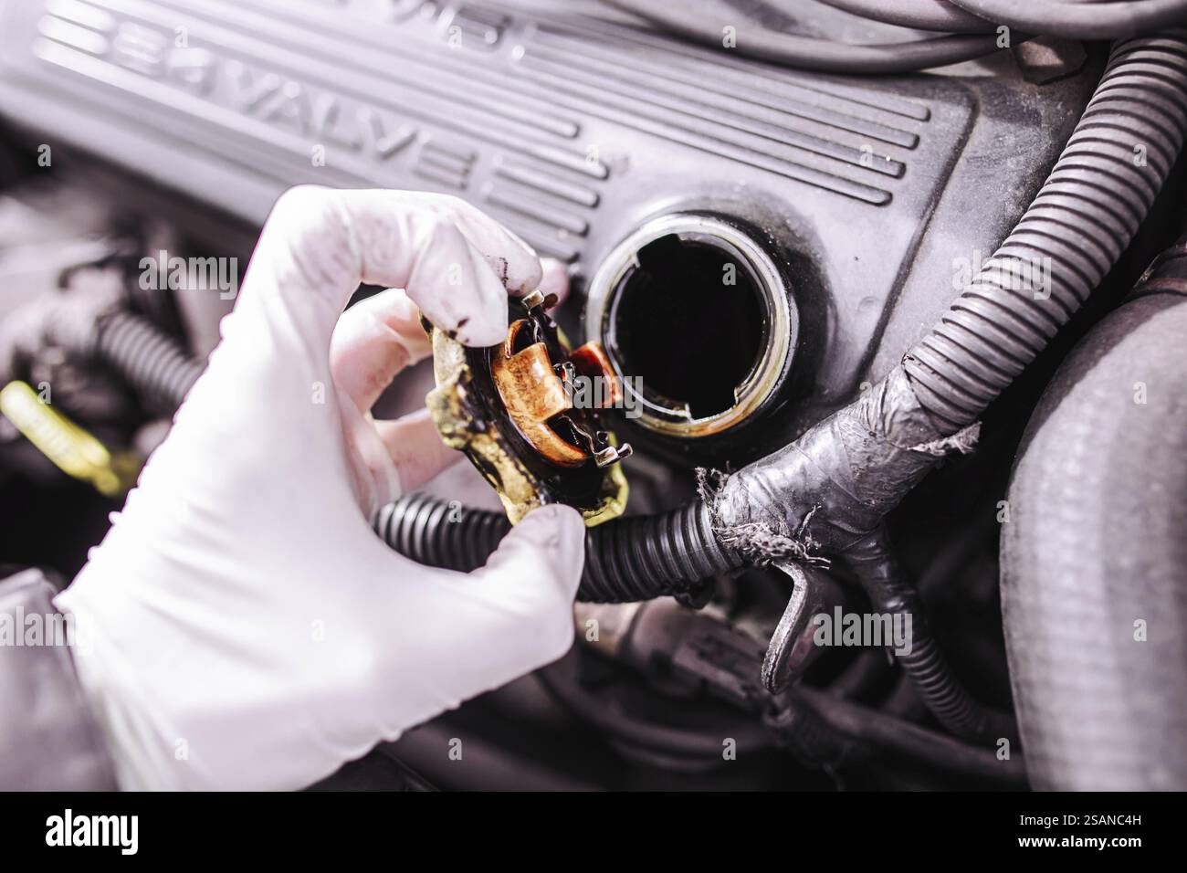 Removing the engine oil cap with a gloved hand in a car engine bay ...