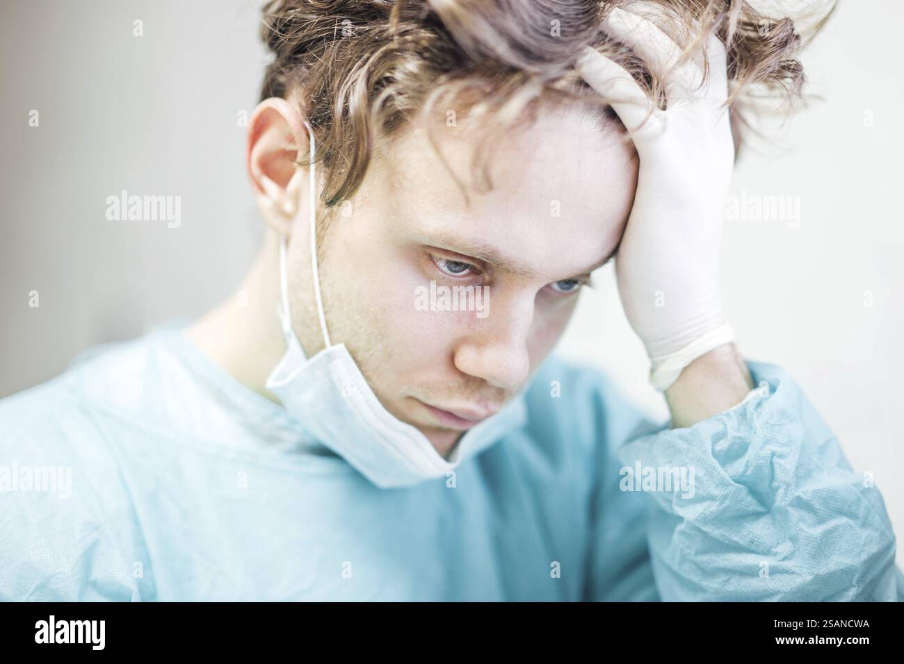A surgeon experiencing stress with hand on forehead, wearing blue ...