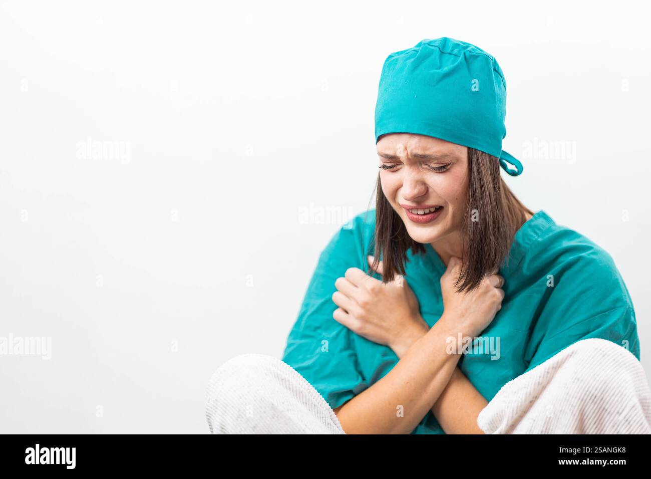 Nurse in teal uniform crying and hugging herself on a white backdrop ...